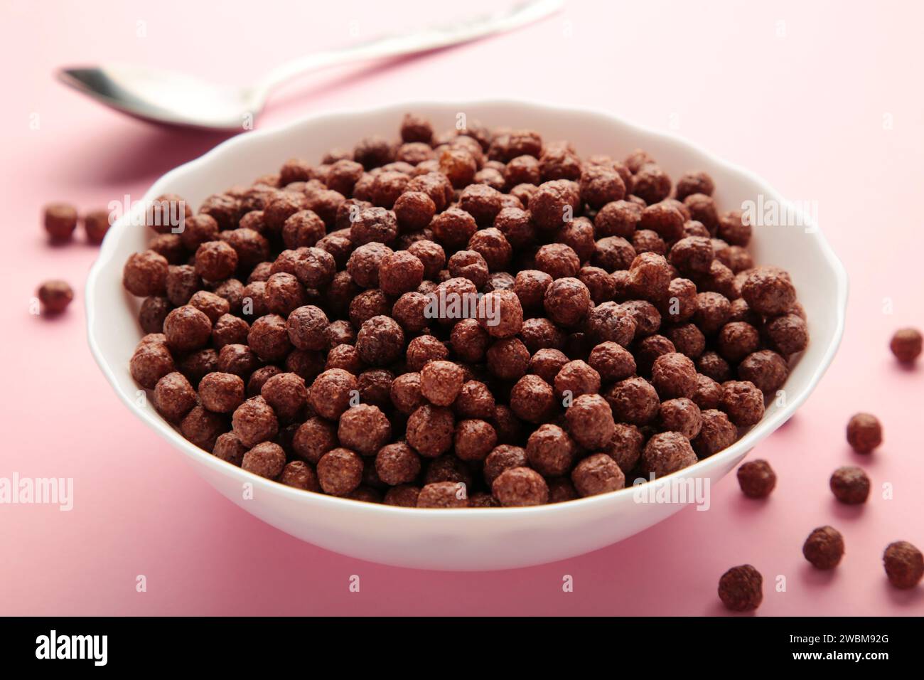 Chocolate cereal corn balls in a white bowl on a pink background. Top ...