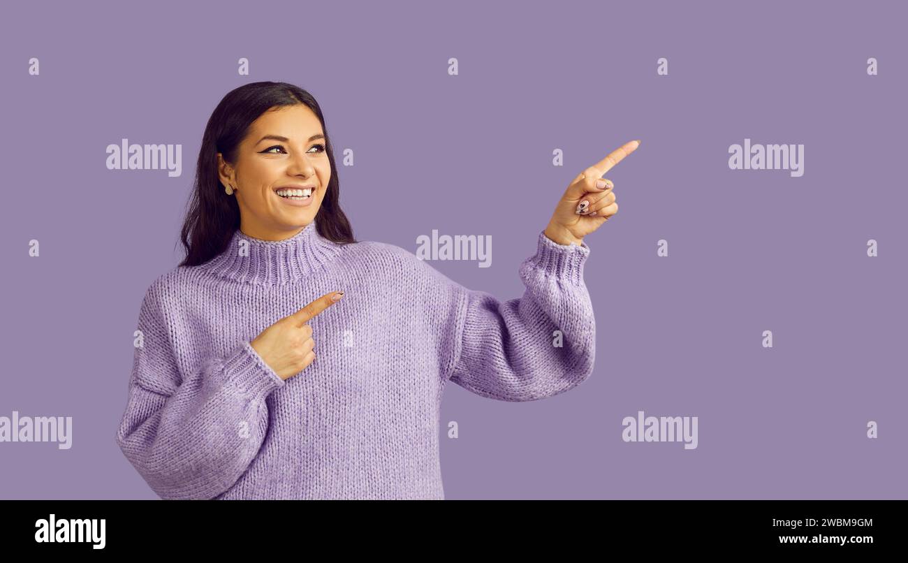 Cheerful good-humored woman in purple sweater smiling and pointing to ...