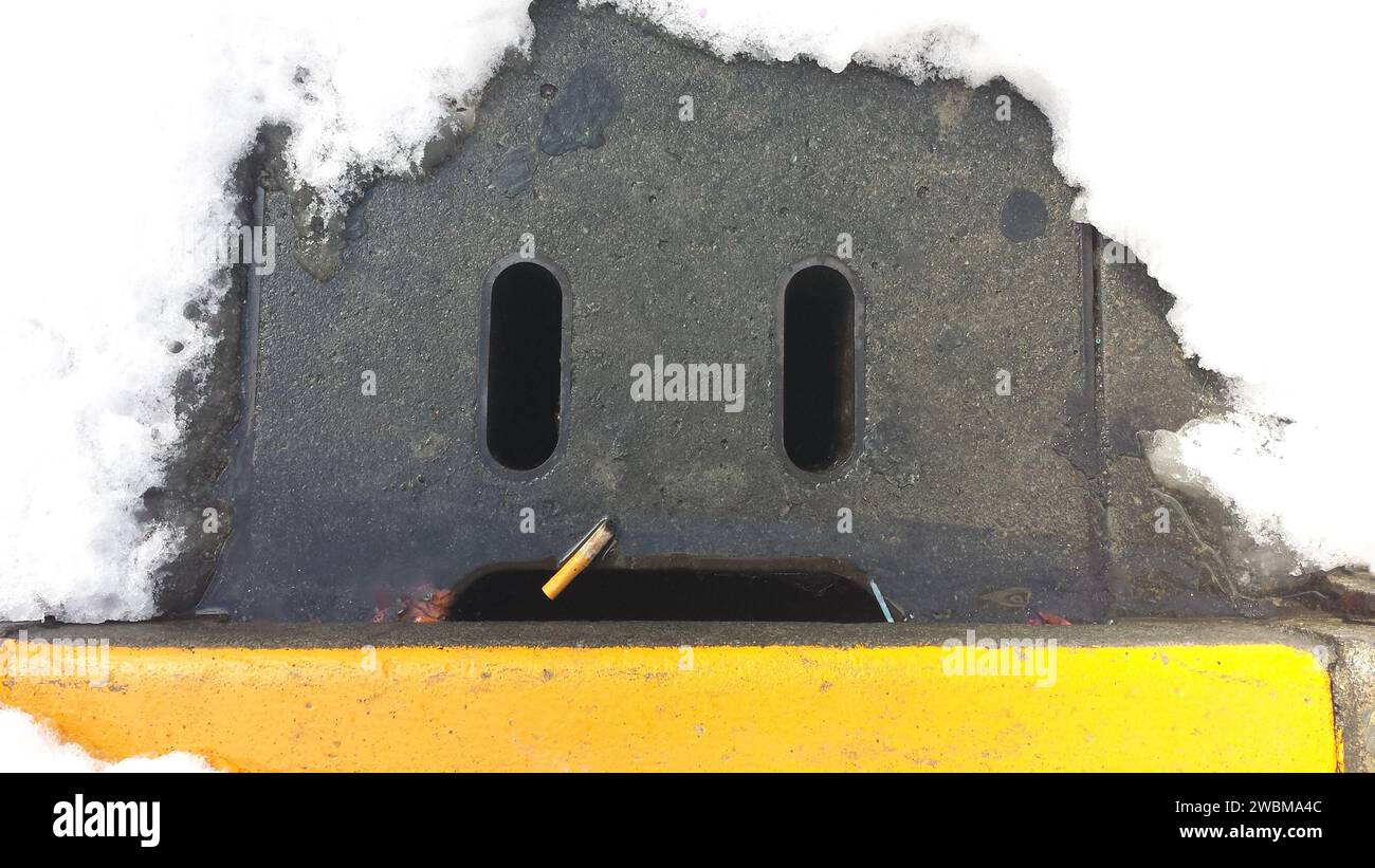 Snow-covered street drain with a visible cigarette butt, highlighting ...