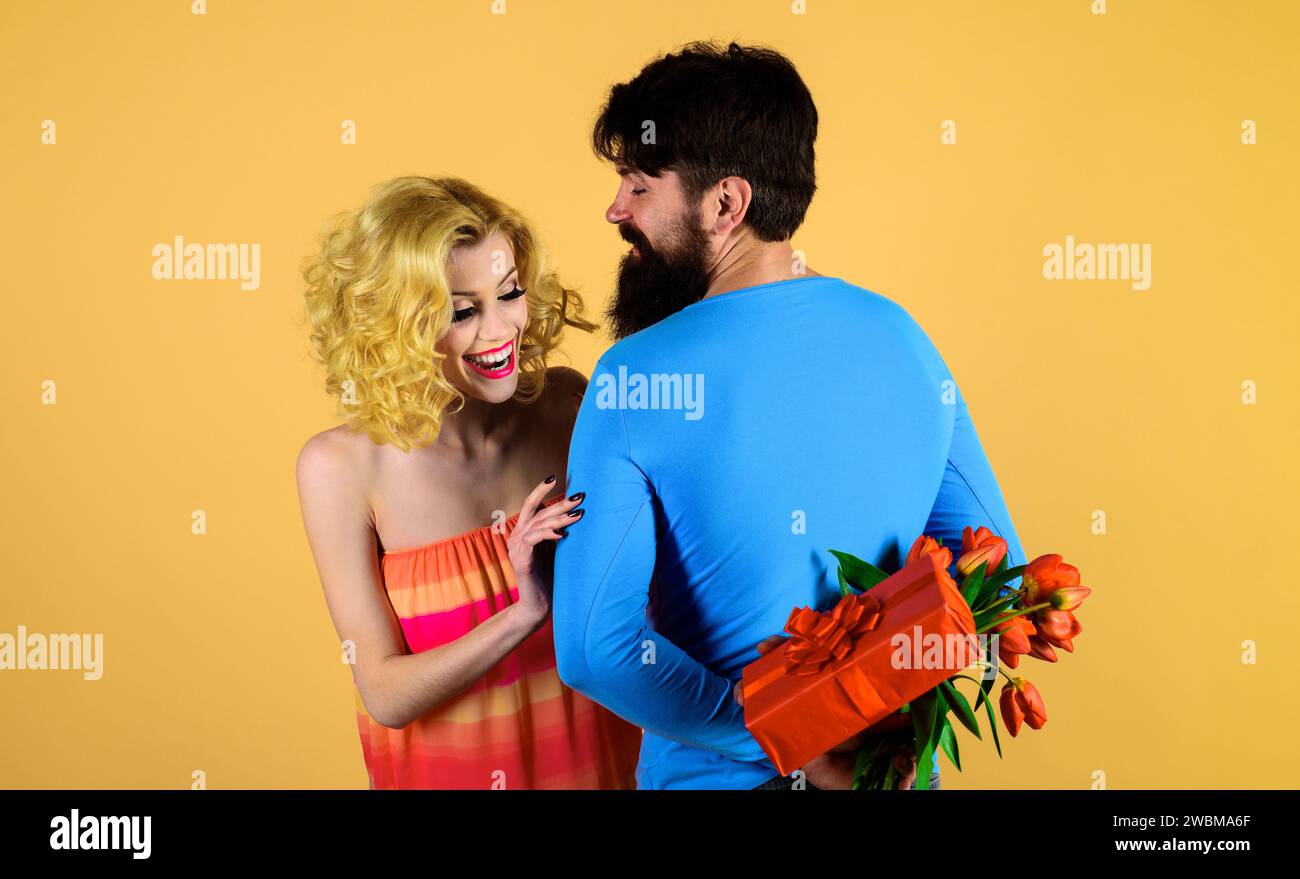 Bearded man with festive gift box and bouquet of tulips behind his back ...