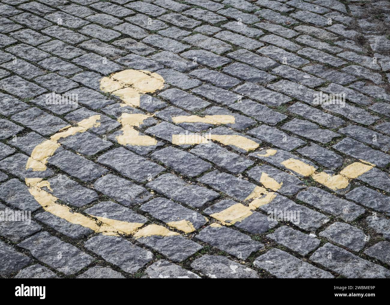 Faded yellow handicapped symbol painted on a cobblestone surface Stock ...