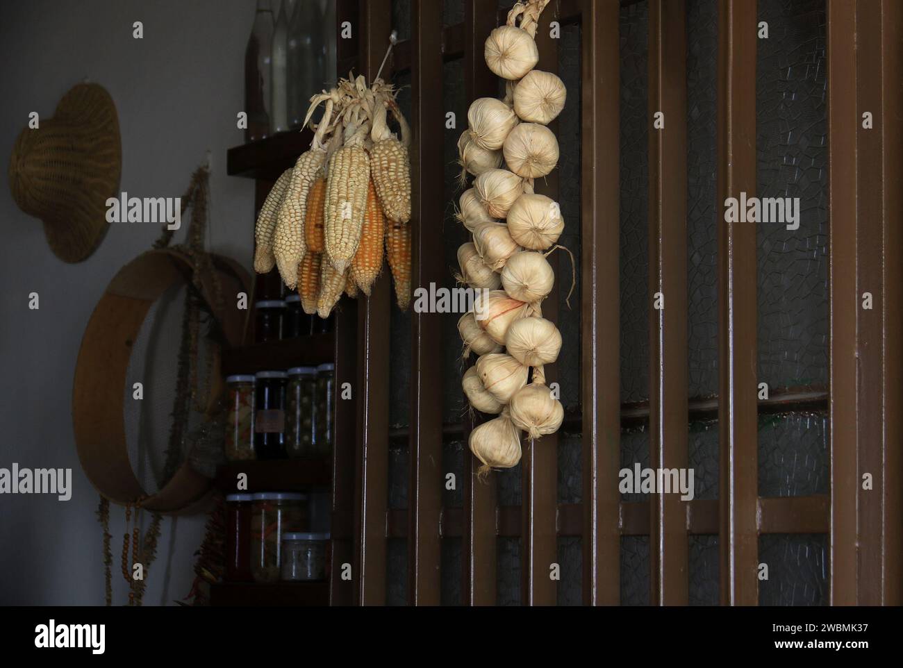 A rural wall with a hanging braid of garlic and a bunch of corn cobs to ...