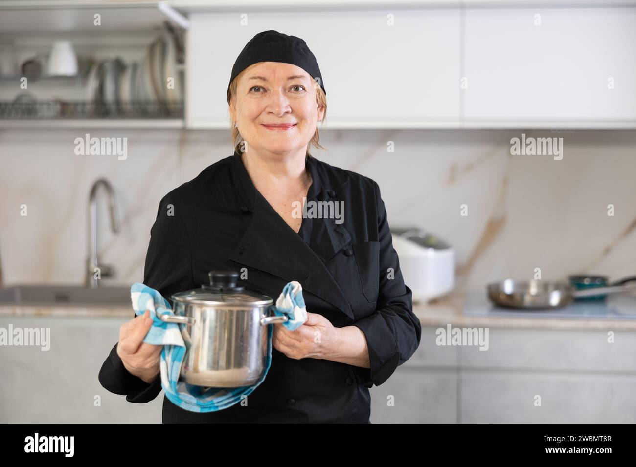Confident mature woman in cook outfit showing around hew kitchen Stock ...