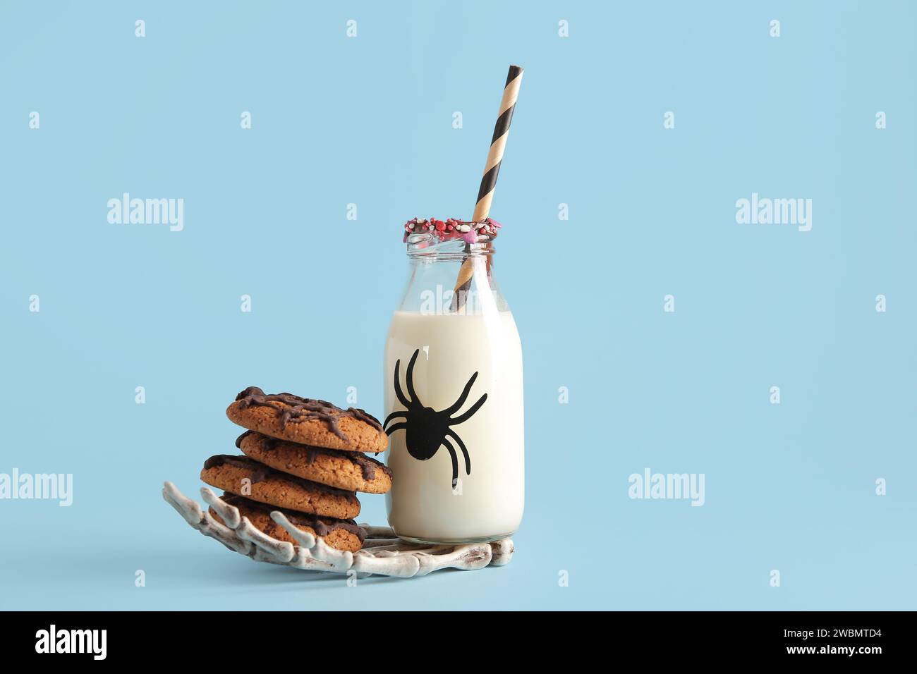 Bottle of milk, skeleton hand and tasty cookies for Halloween on blue ...