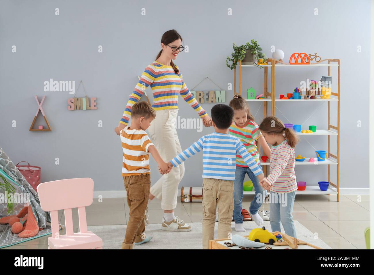 Little children with nursery teacher doing round dance in kindergarten ...