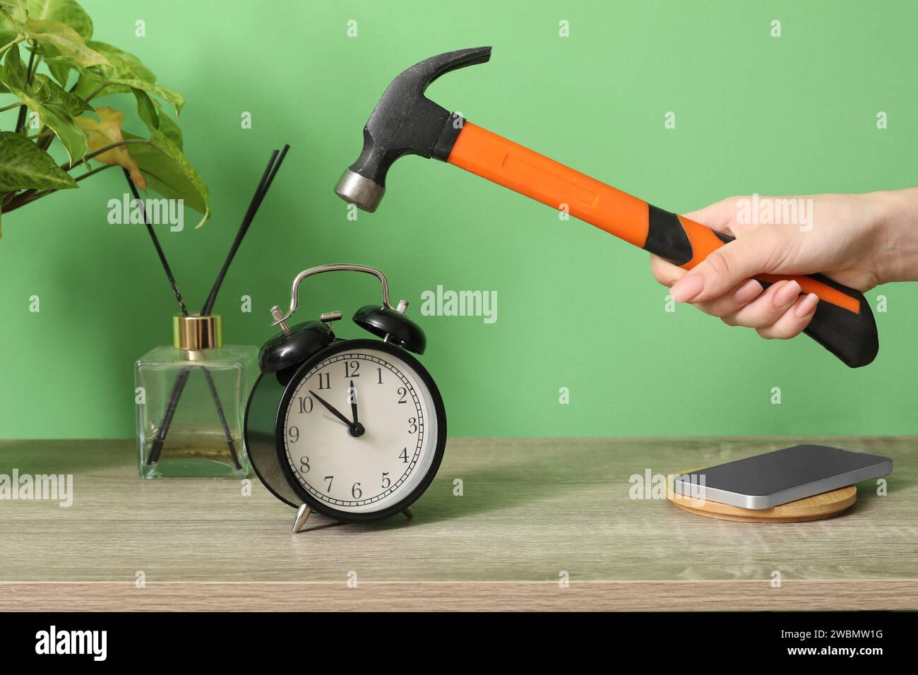 Woman breaking alarm clock with hammer on table near green wall Stock ...