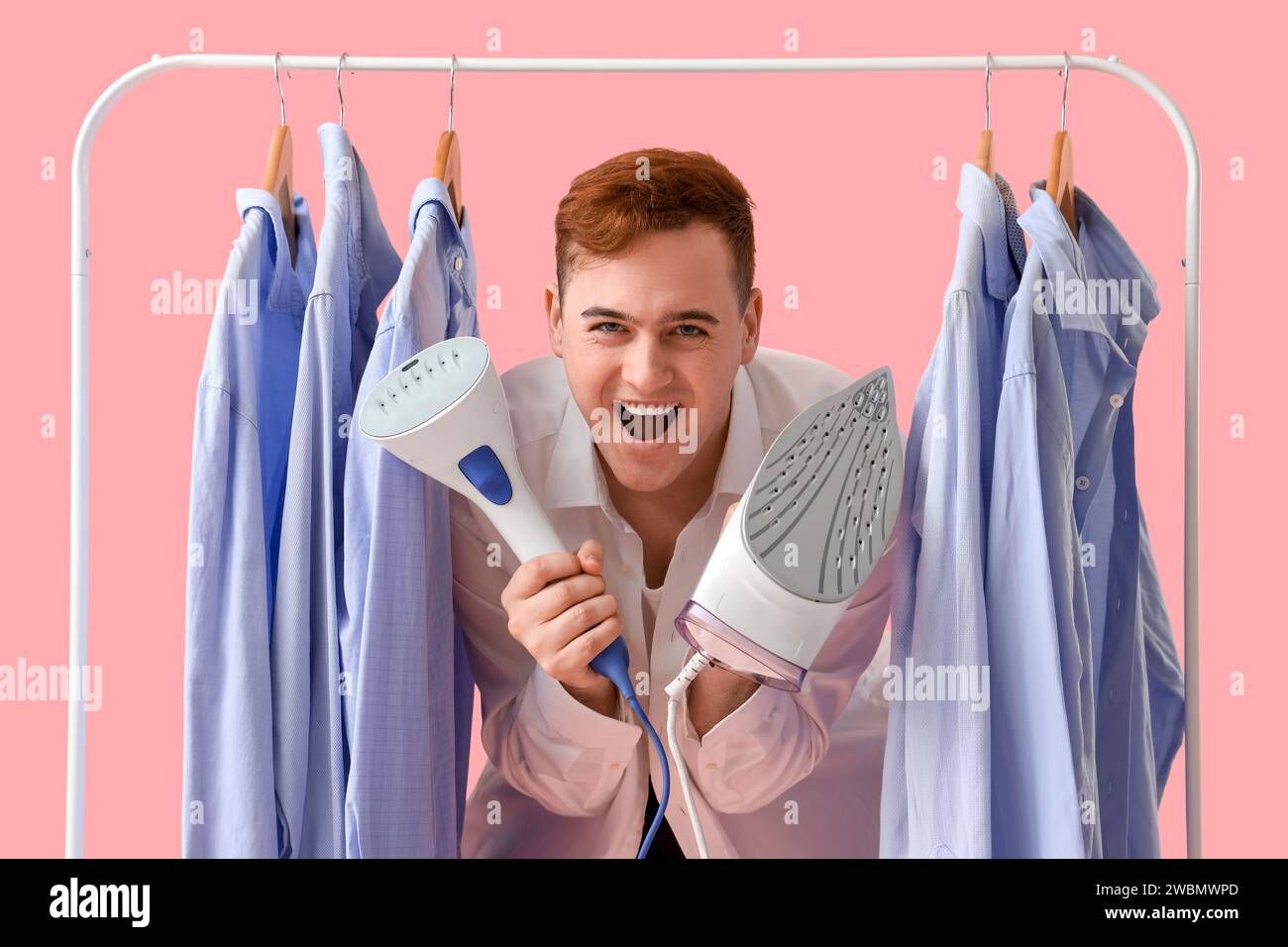 Excited young man with electric iron and garment steamer near clothes ...