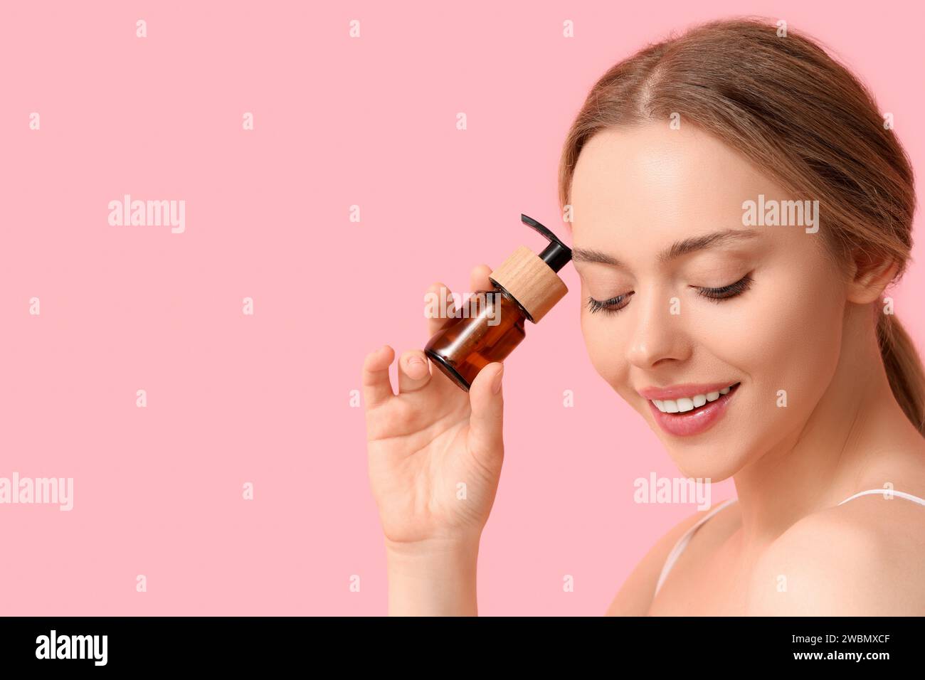 Beautiful young woman with bottle of cosmetic product on pink ...