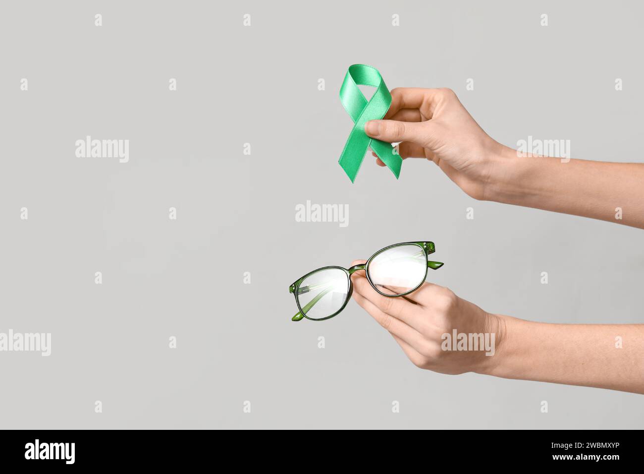 Female hands with green ribbon and eyeglasses on grey background ...