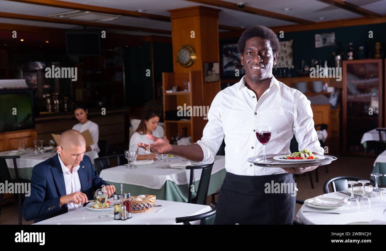 Hospitable african american waiter greeting guests in restaurant Stock ...