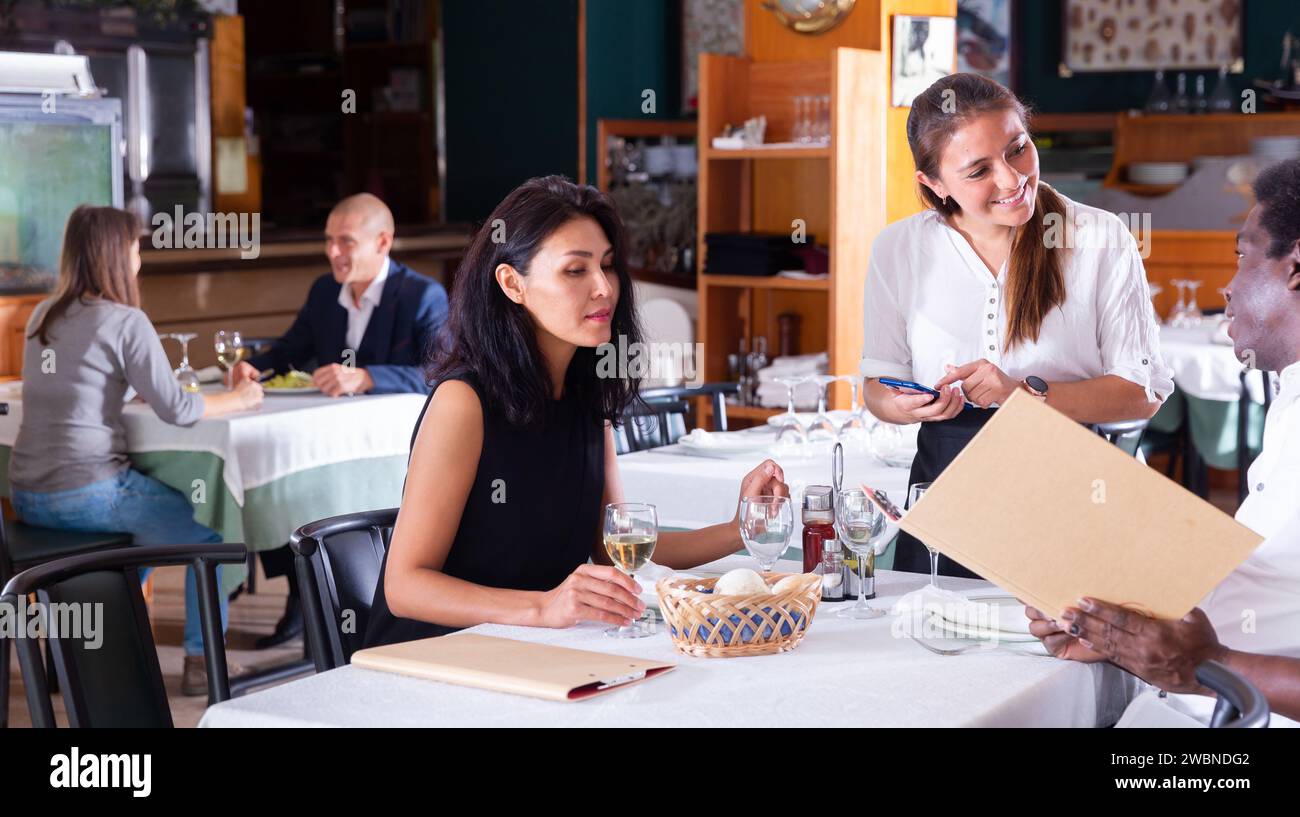 Polite young waitress helping with menu to African American Stock Photo ...