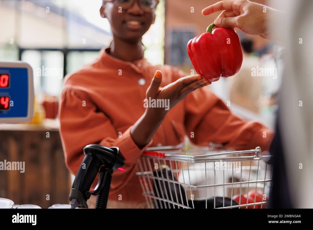 Close-up of black woman giving fresh red bell pepper to shopkeeper for ...