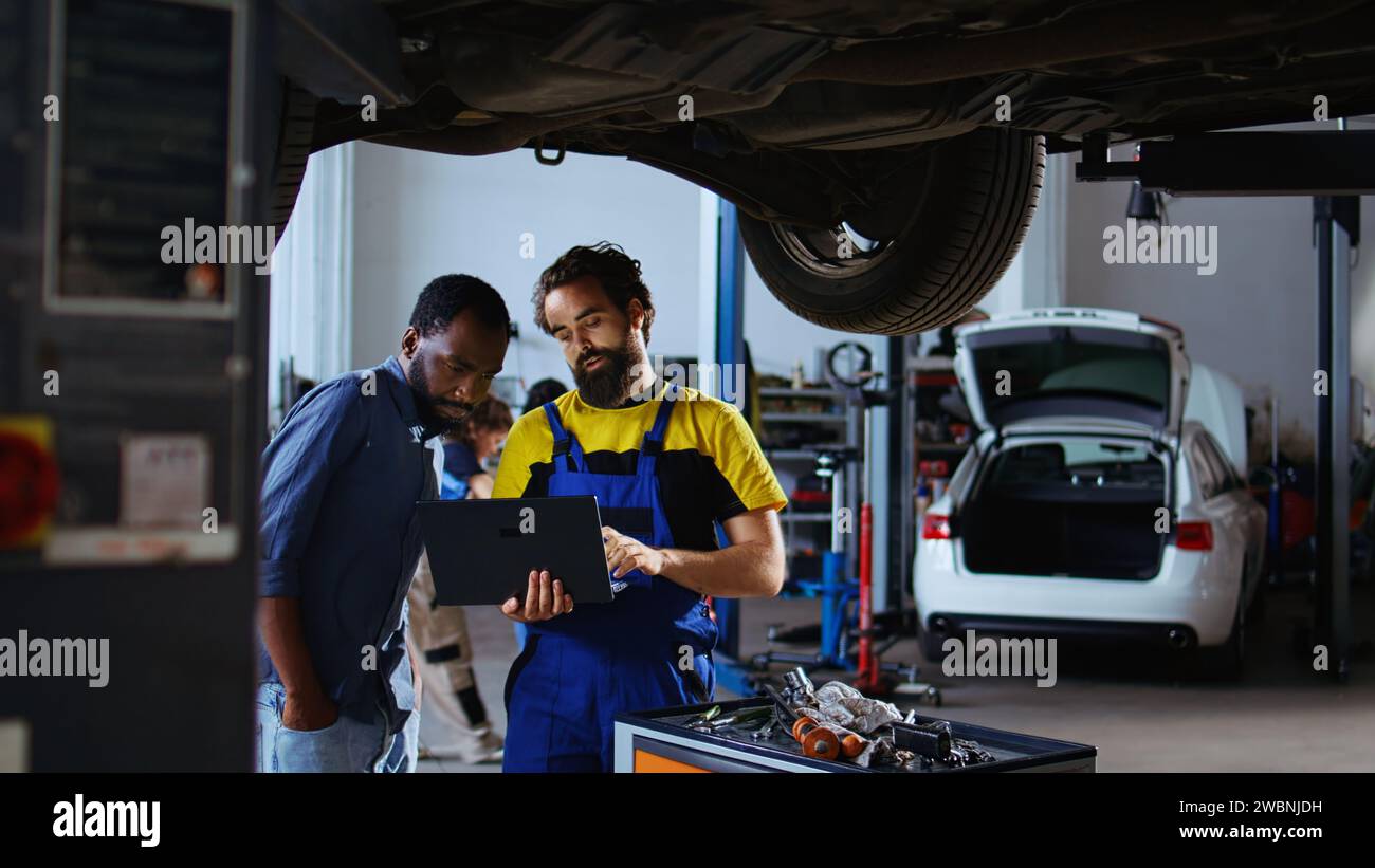 Trained mechanic and customer standing underneath car in garage using ...