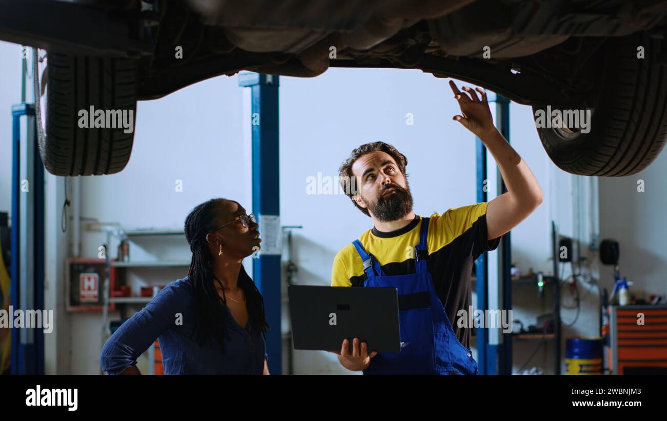 Mechanic in auto repair shop standing with customer underneath ...