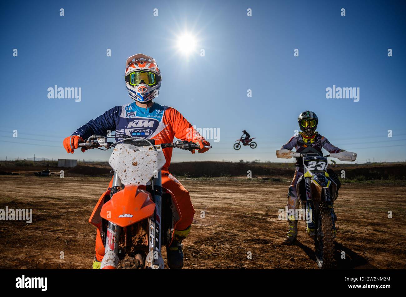 Backlight of two front facing motocross riders posing with another ...