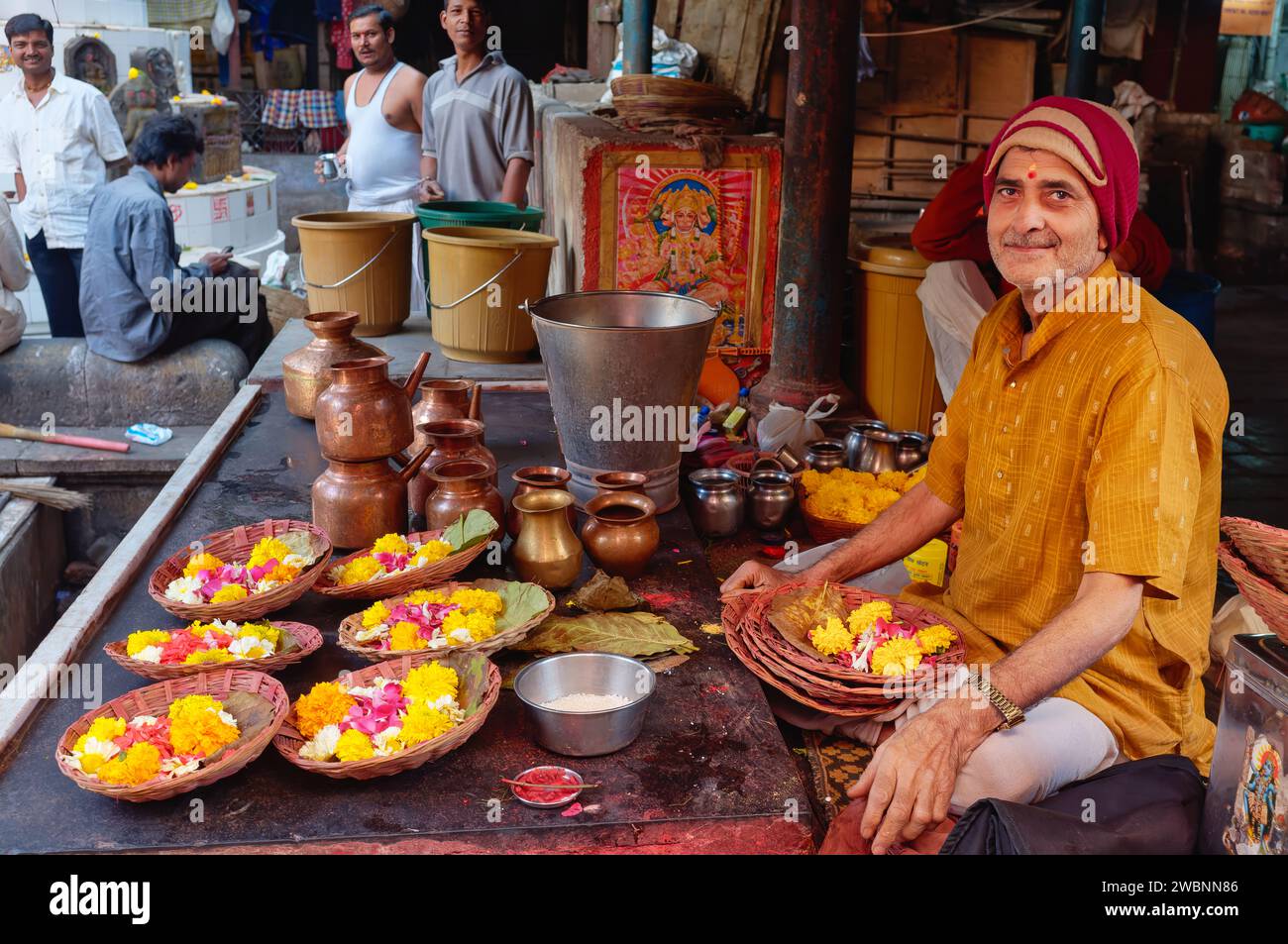 A Hindu priest sits ready to hand out trays of flower offerings to ...