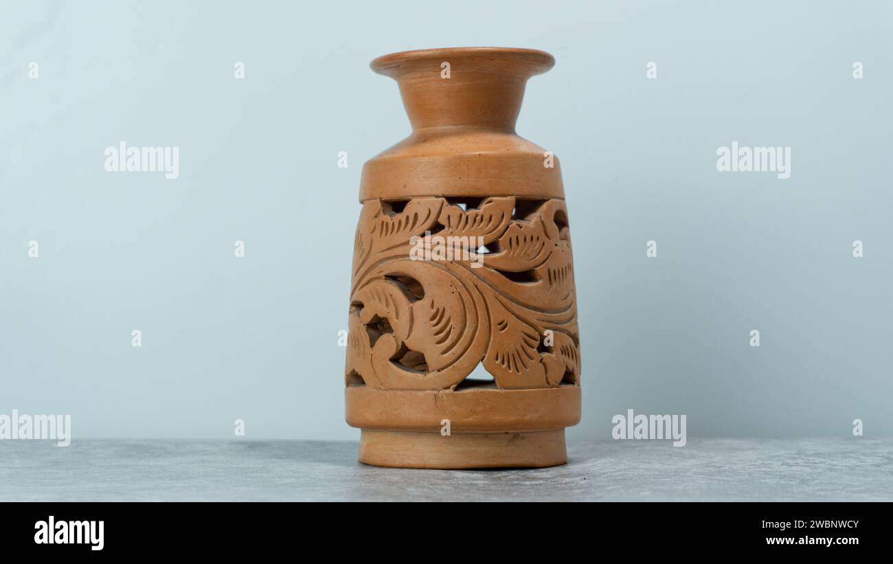 A clay jug with reliefs on the sides is placed on a gray table with a ...