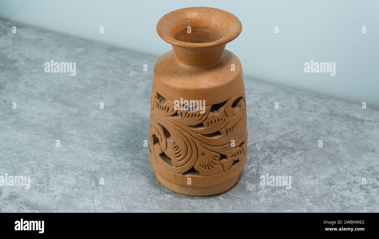 A clay jug with reliefs on the sides is placed on a gray table with a ...