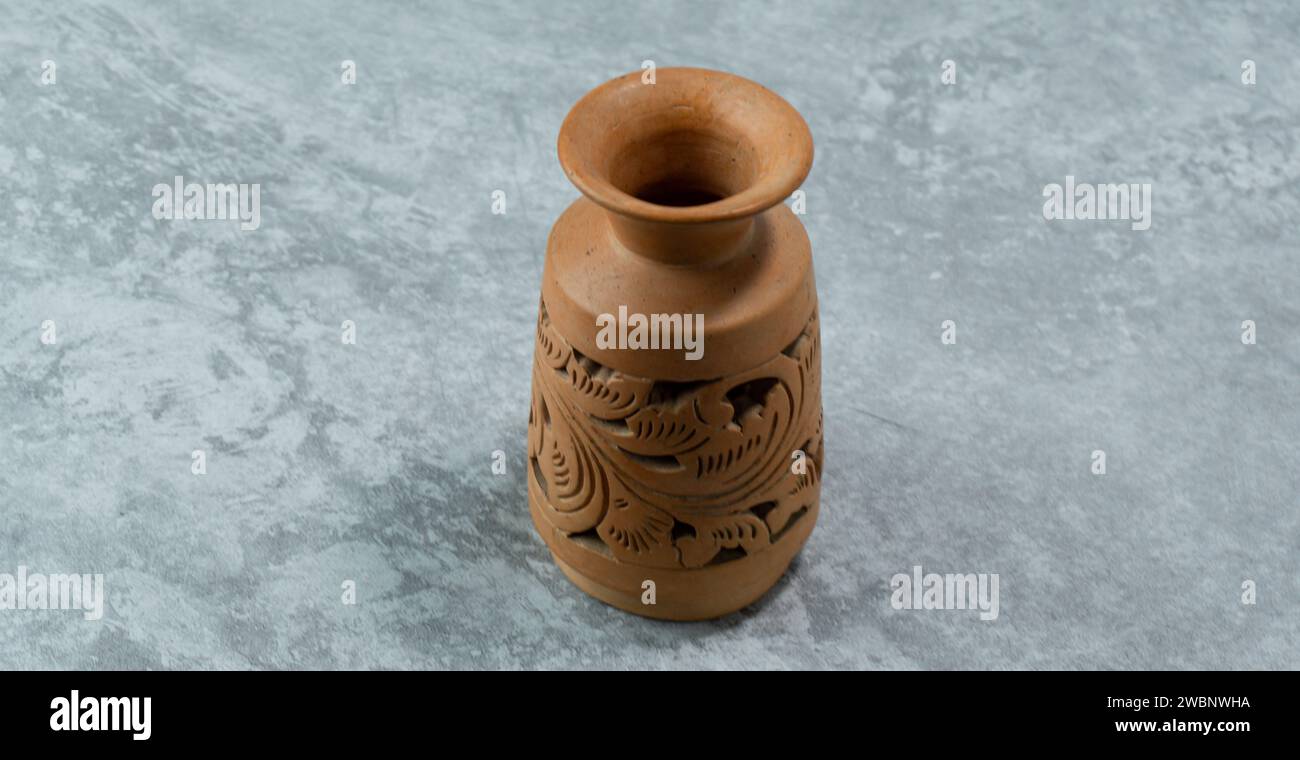 A clay jug with reliefs on the sides is placed on a gray table with a ...