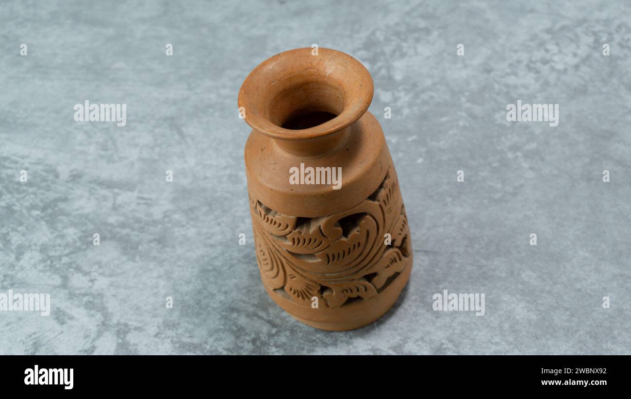 A clay jug with reliefs on the sides is placed on a gray table with a ...