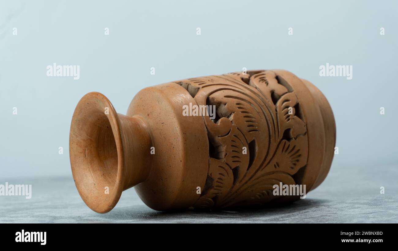 A clay jug with reliefs on the sides is placed on a gray table with a ...