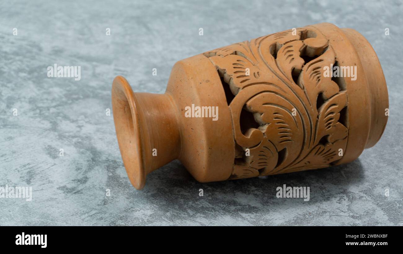 A clay jug with reliefs on the sides is placed on a gray table with a ...
