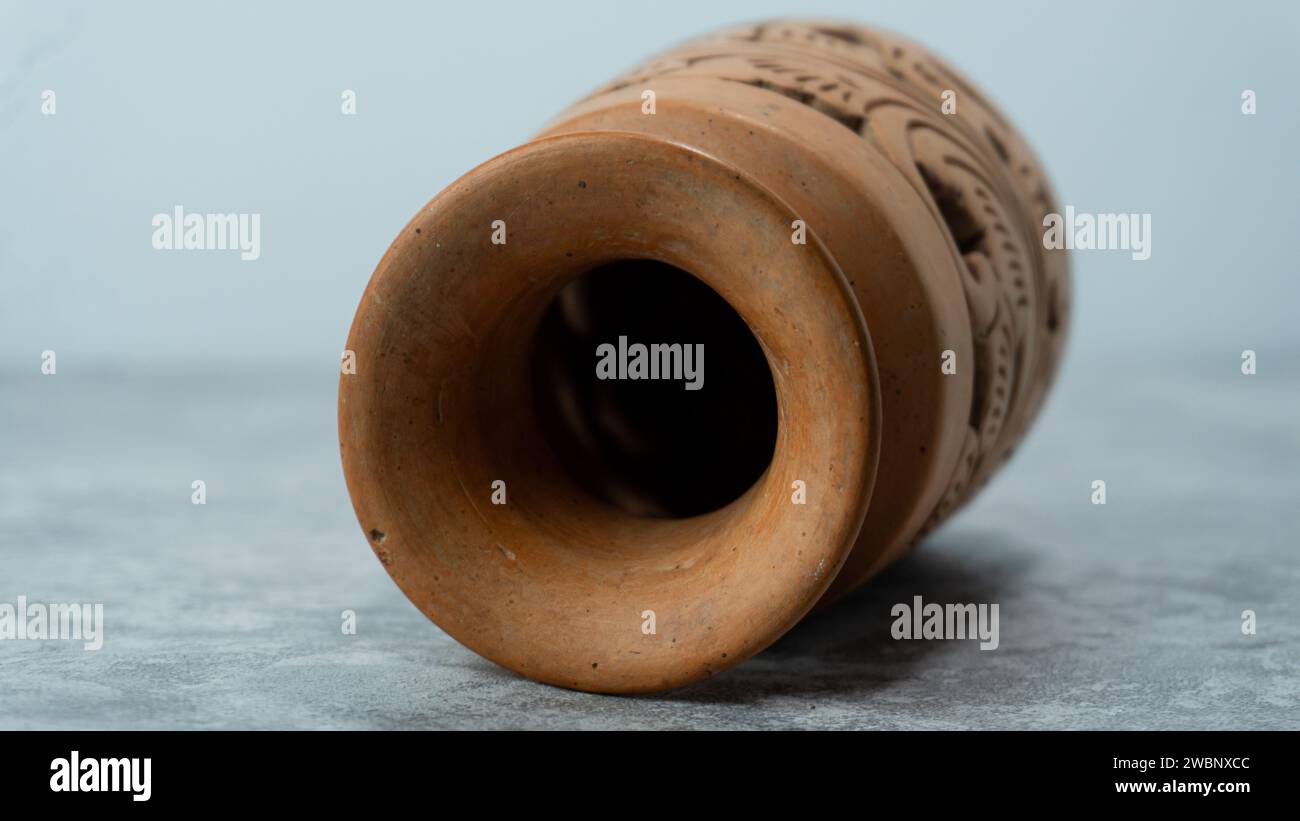 A clay jug with reliefs on the sides is placed on a gray table with a ...