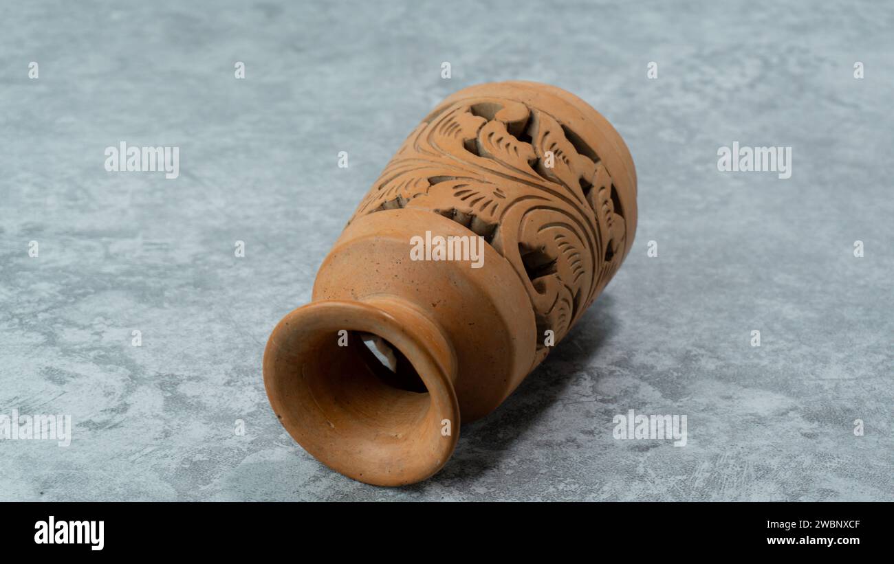 A clay jug with reliefs on the sides is placed on a gray table with a ...