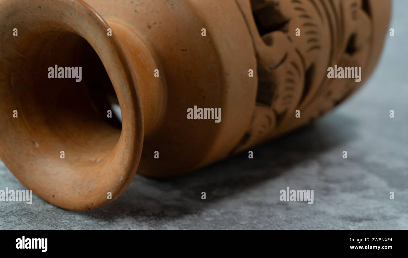 A clay jug with reliefs on the sides is placed on a gray table with a ...