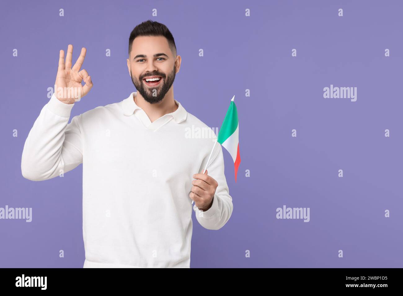 Young man with flag of Italy showing ok gesture on purple background ...