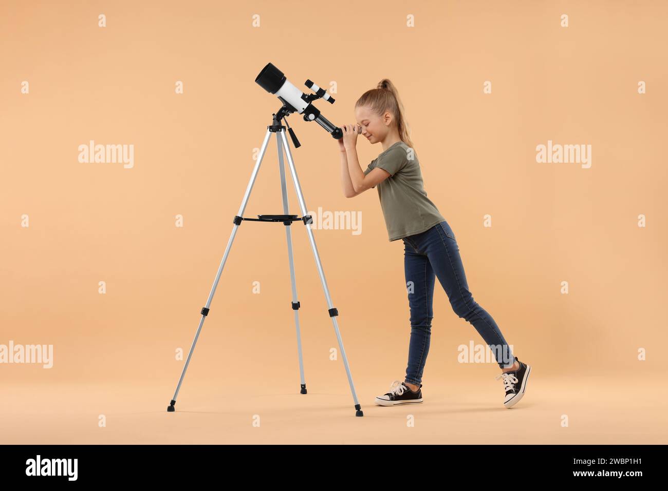 Little girl looking at stars through telescope on beige background ...