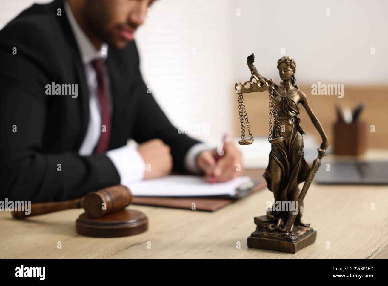 Lawyer working at table in office, focus on statue of Lady Justice ...