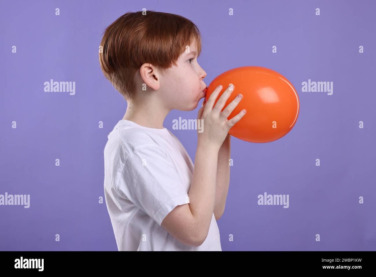 Boy inflating orange balloon on violet background Stock Photo - Alamy