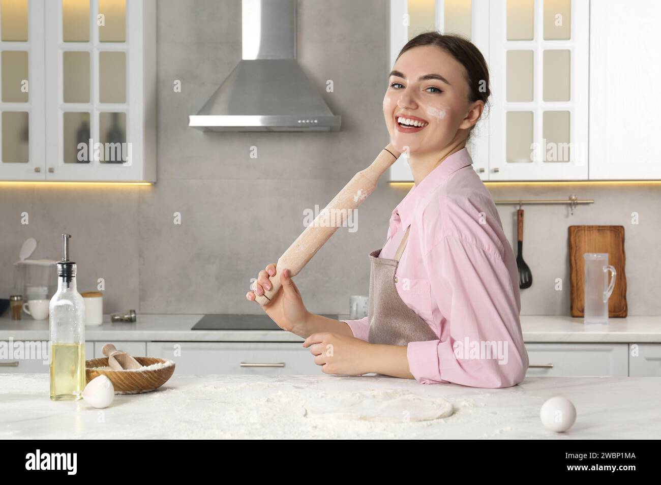 Smiling woman with soiled face holding rolling pin at messy table in ...