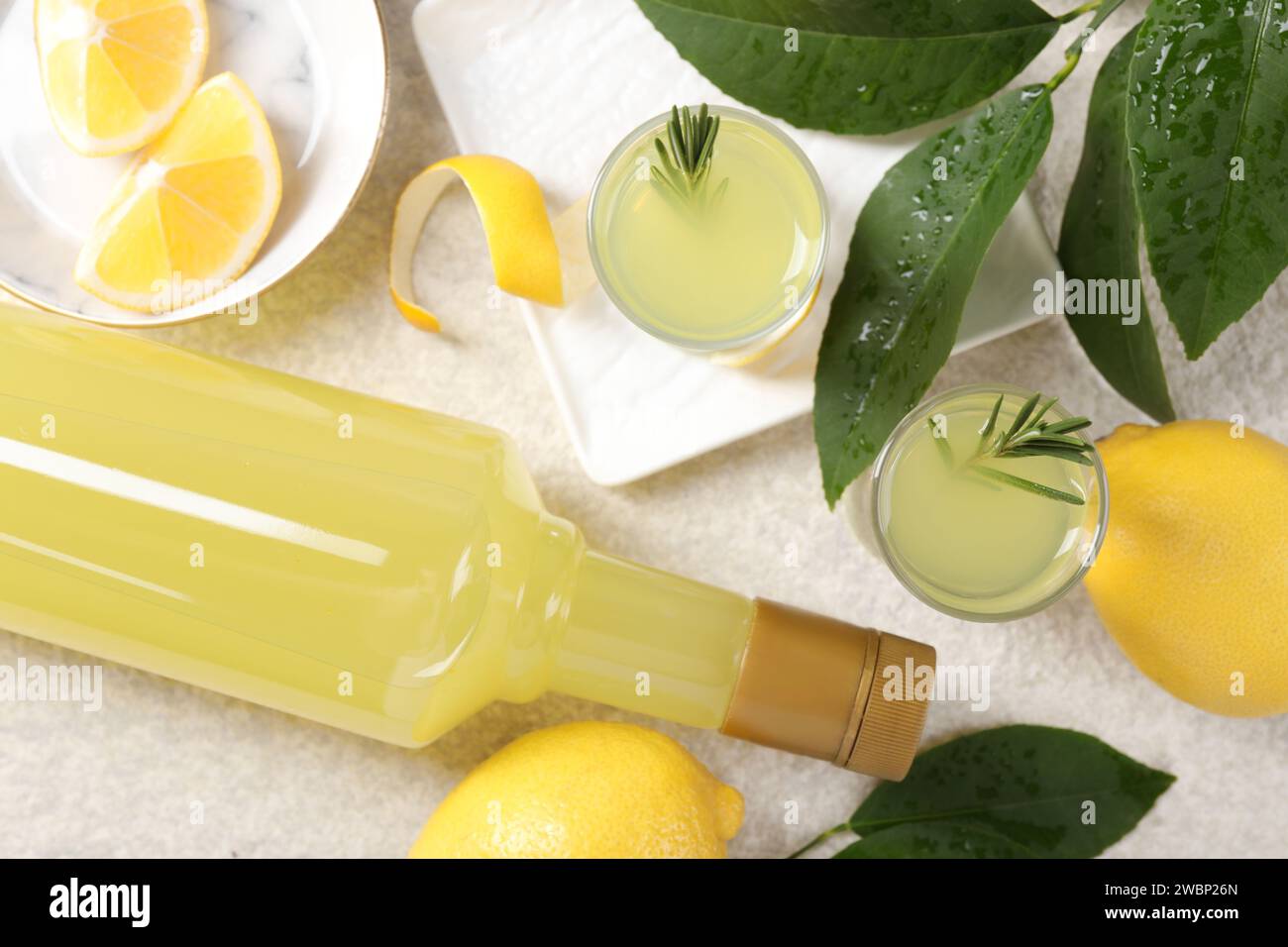 Tasty limoncello liqueur, lemons and green leaves on light textured ...