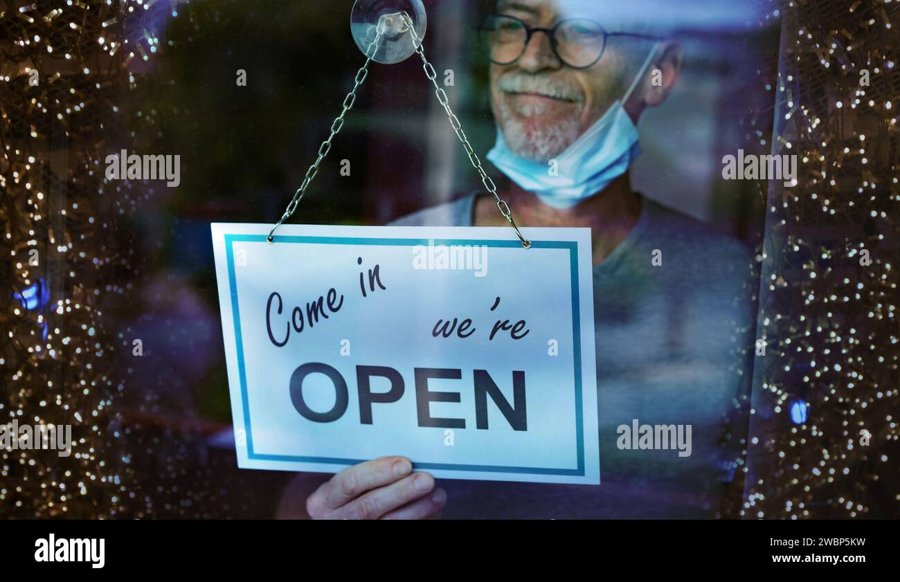 Store owner hanging come in we're open sign on window; light effect ...