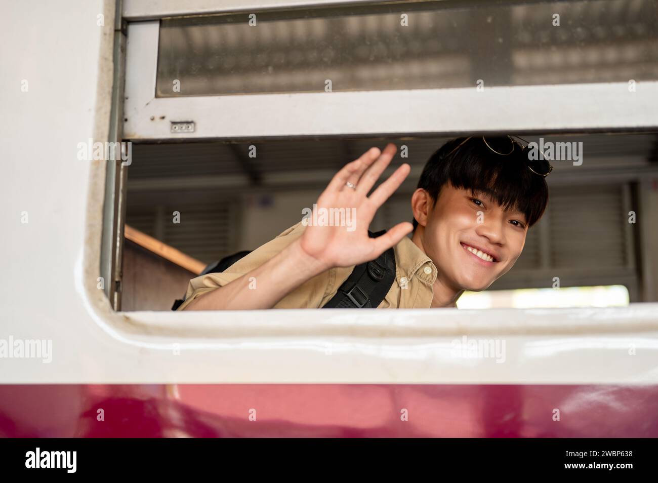 A happy, excited young Asian man is on a train, sitting by the window ...