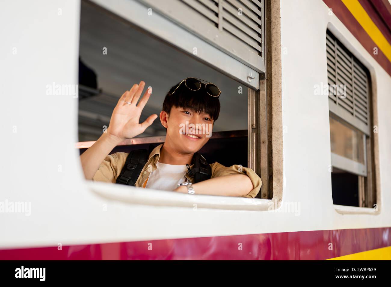 A happy, excited young Asian man is on a train, sitting by the window ...