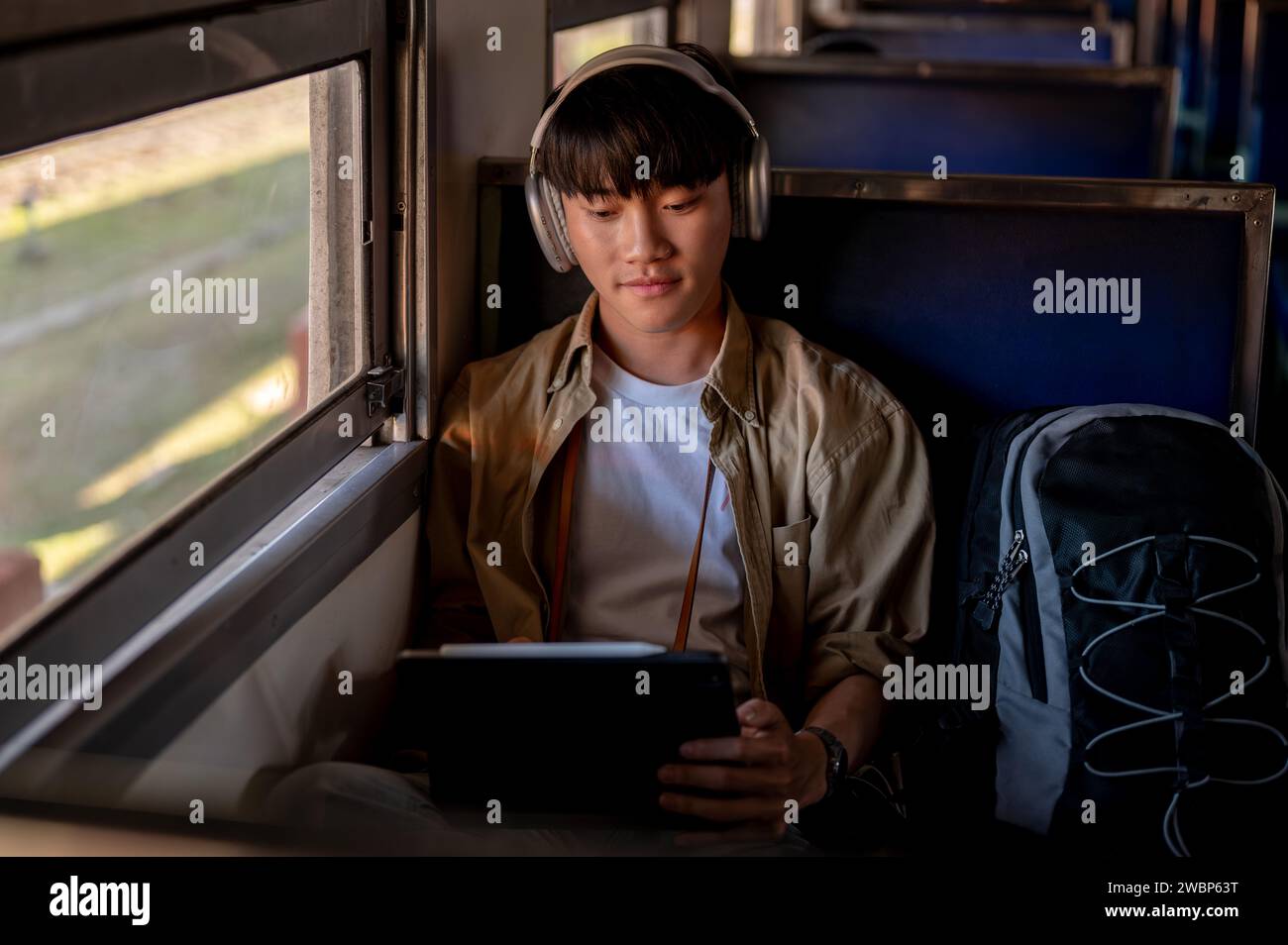 A happy and relaxed young Asian male traveler is listening to music on ...