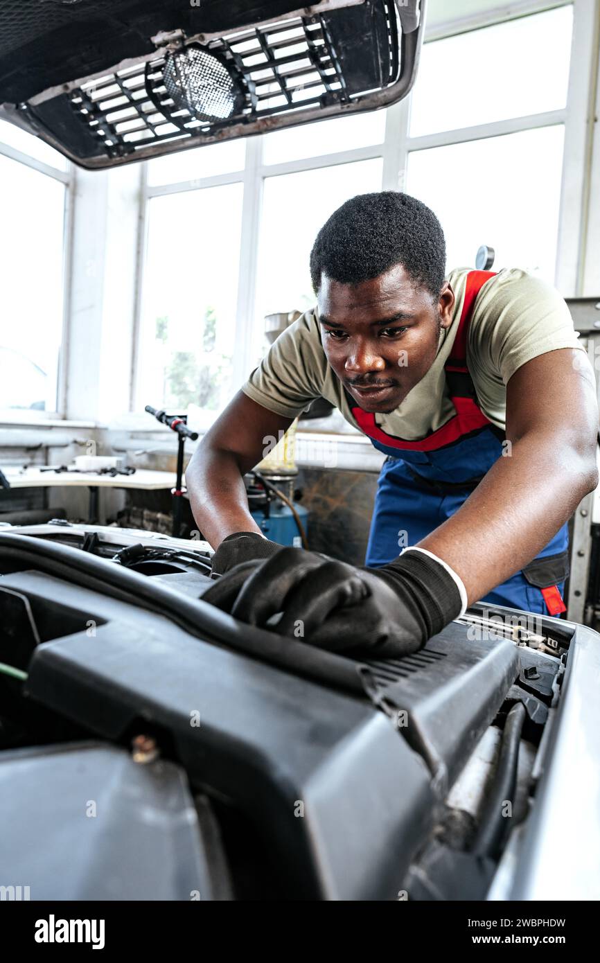 Young African man working under the hood of car fixing engine in auto ...