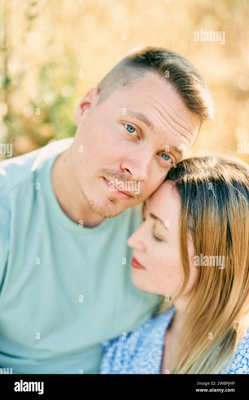 Guy touches girl head with his cheek while hugging her while sitting on ...