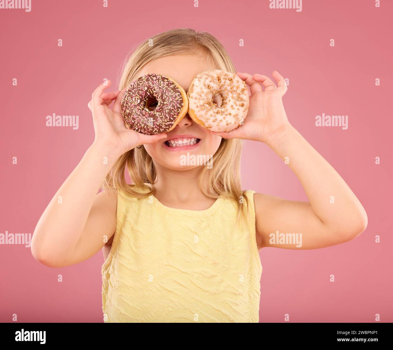 Child, donut over eyes and smile in studio with sweet snack in hands on ...
