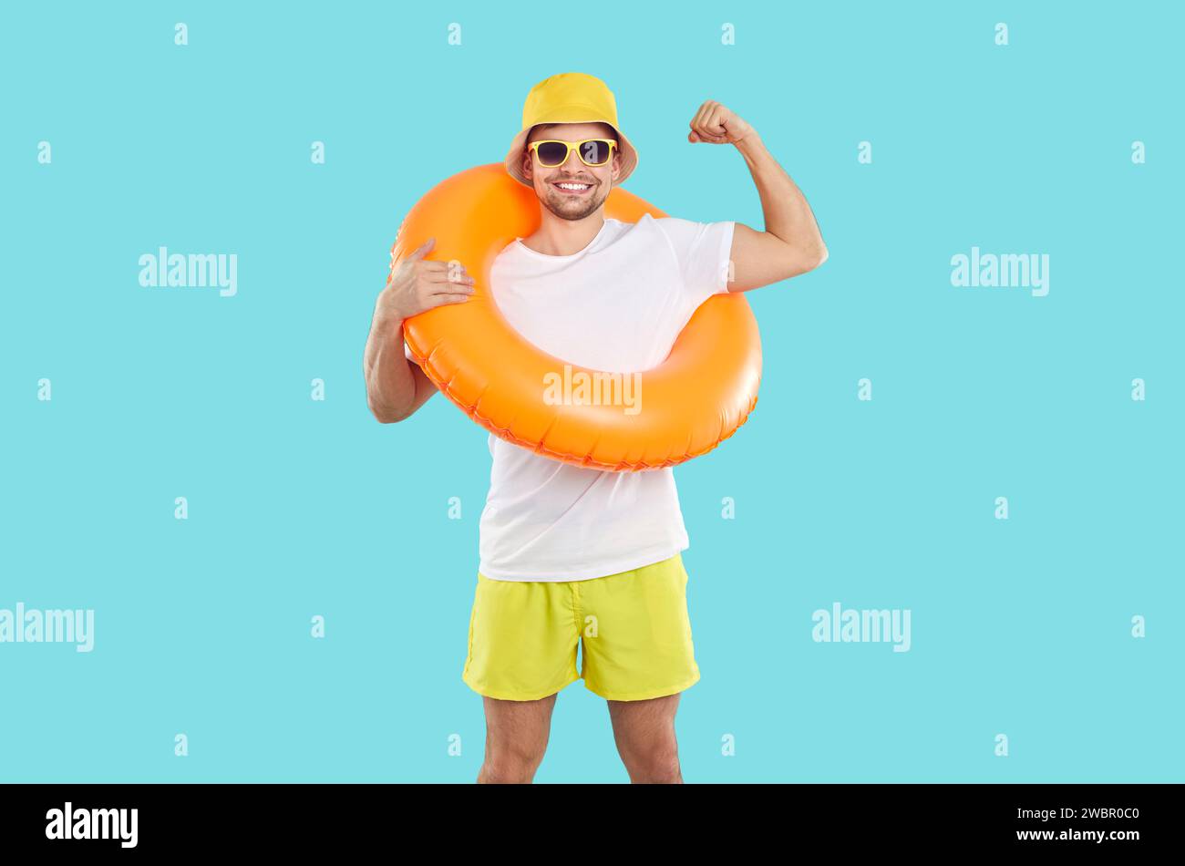 Cheerful man with inflatable swimming circle shows biceps on light blue ...