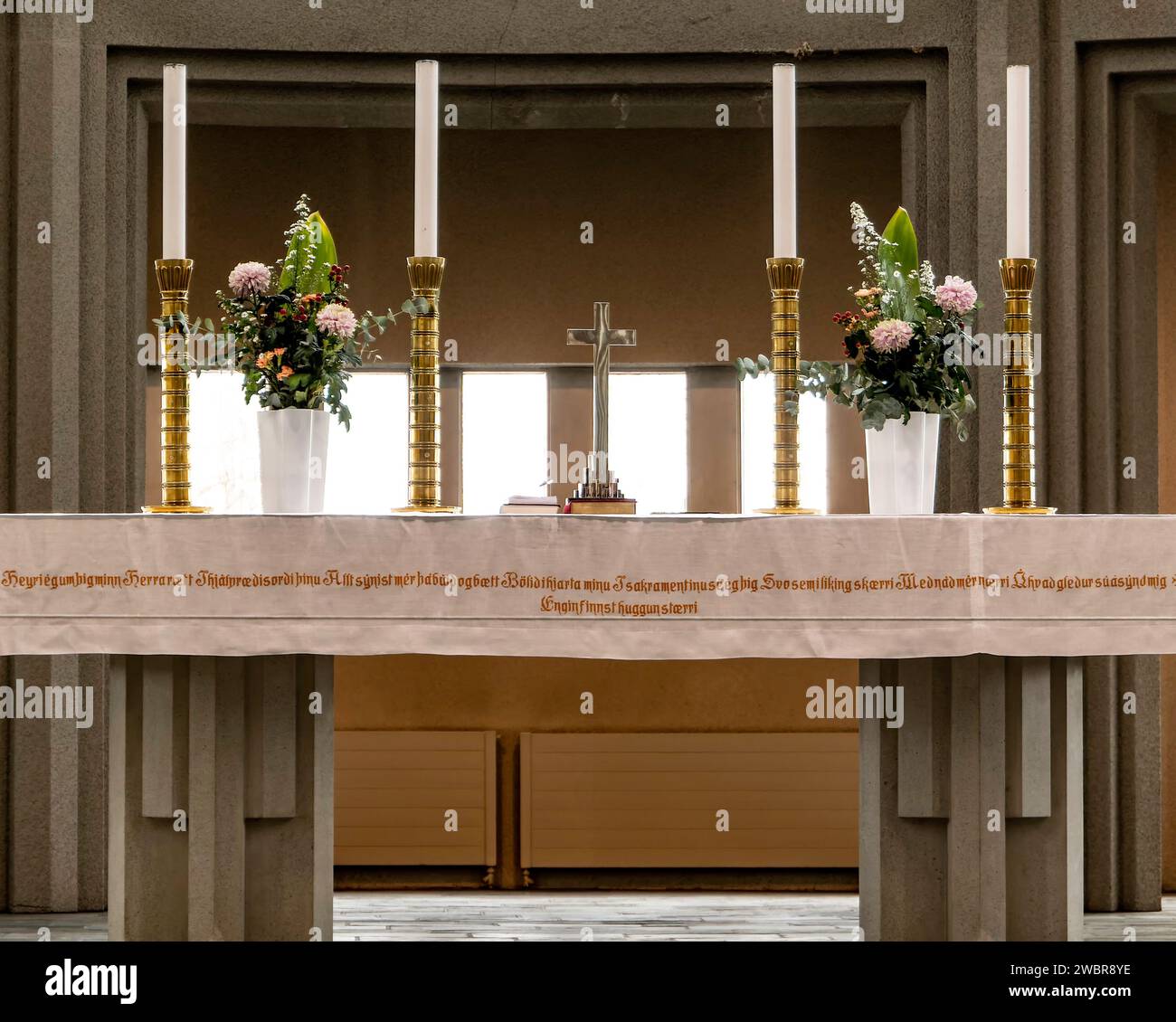 Cross placed on stone surface with inscription near flowers and candles ...