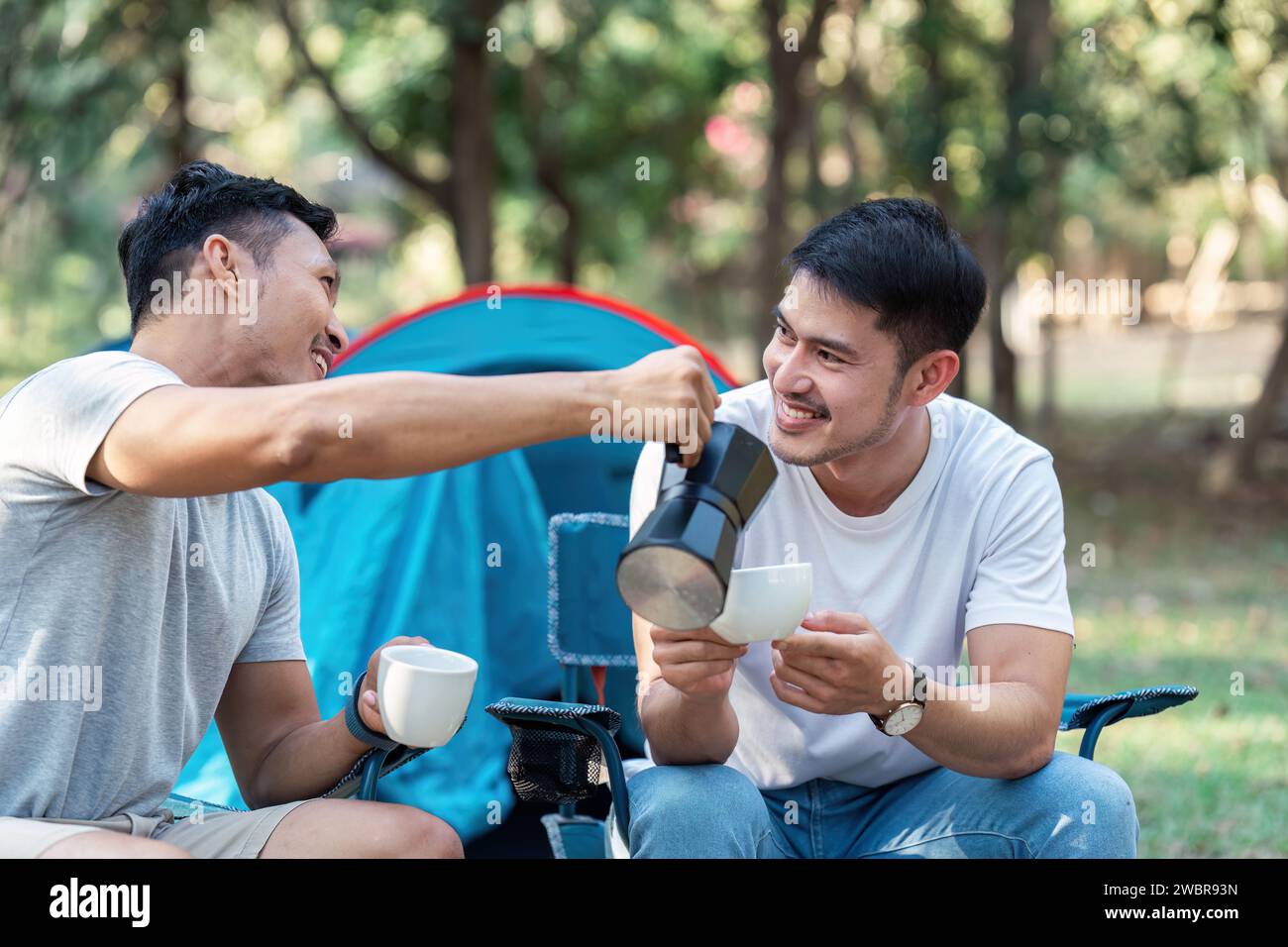 Gay LGBTQIA couple sitting on picnic chair drinking tea and coffee ...