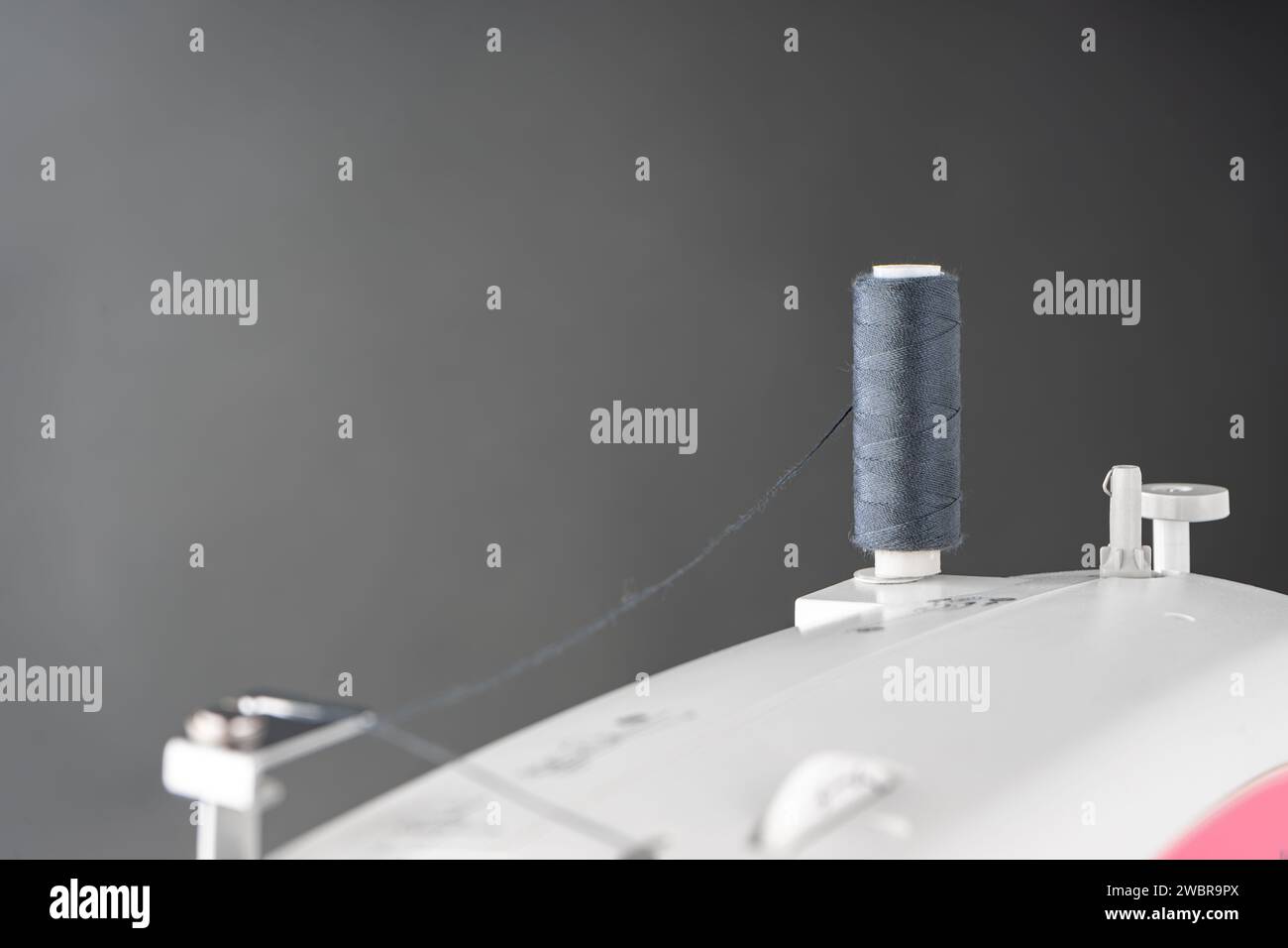 Spool of gray sewing thread stands on top of a white modern sewing ...