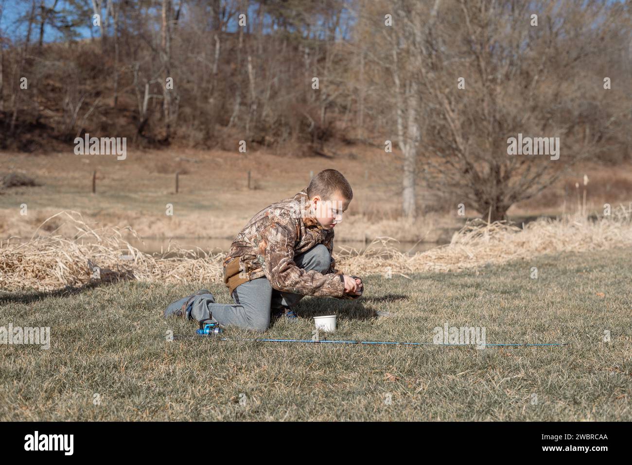 Boy putting work on fishing rod near pond Stock Photo - Alamy
