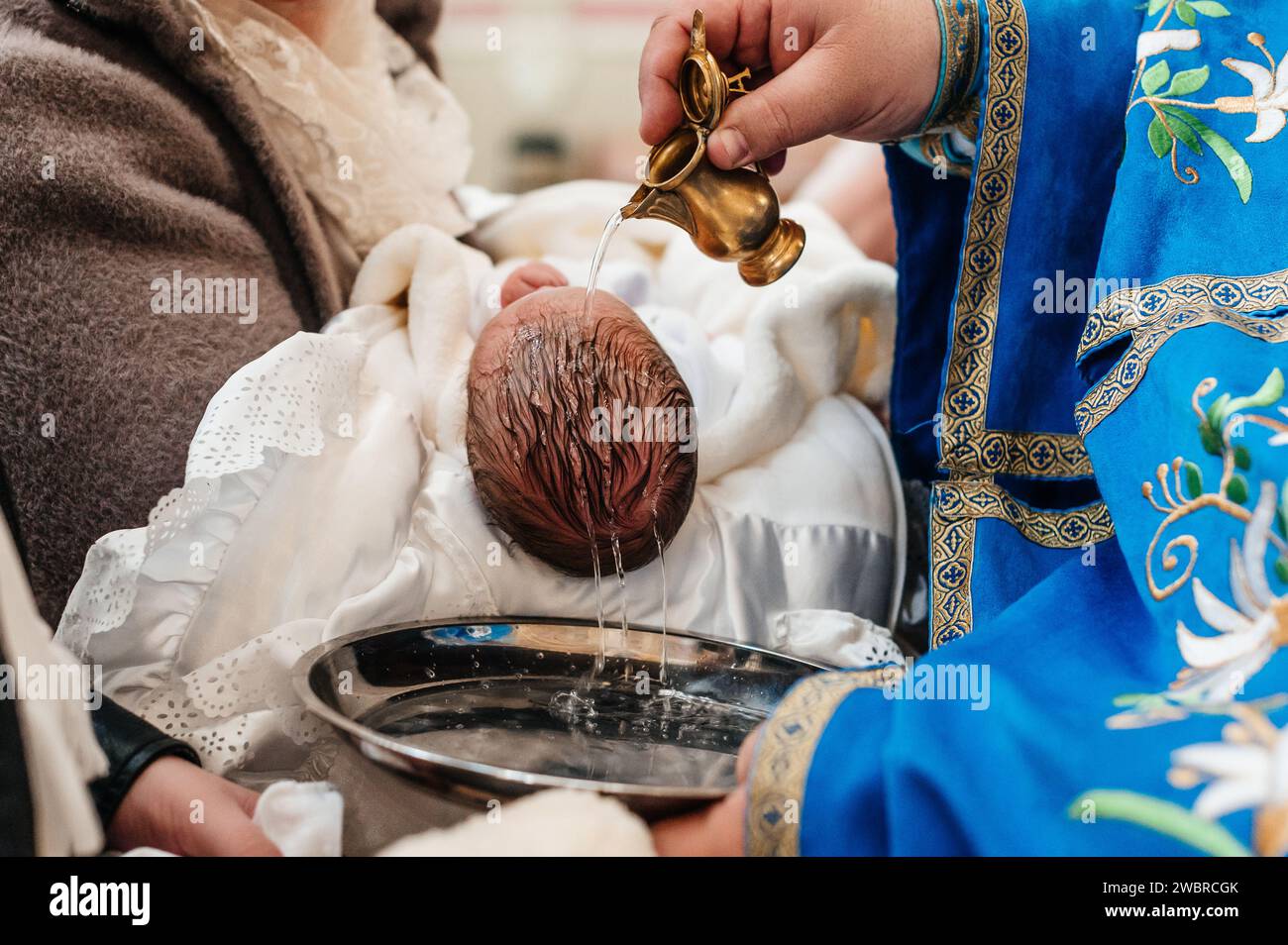A priest pours water on the head of a small child during the Christian rite of baptism in the ...
