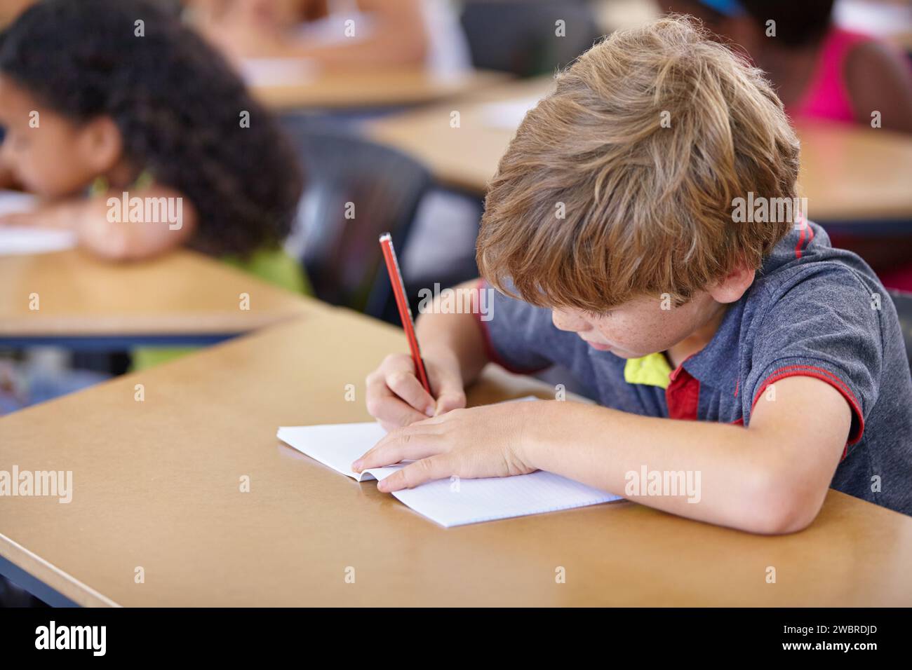 School, boy and kid writing in notebook in classroom, desk and studying ...