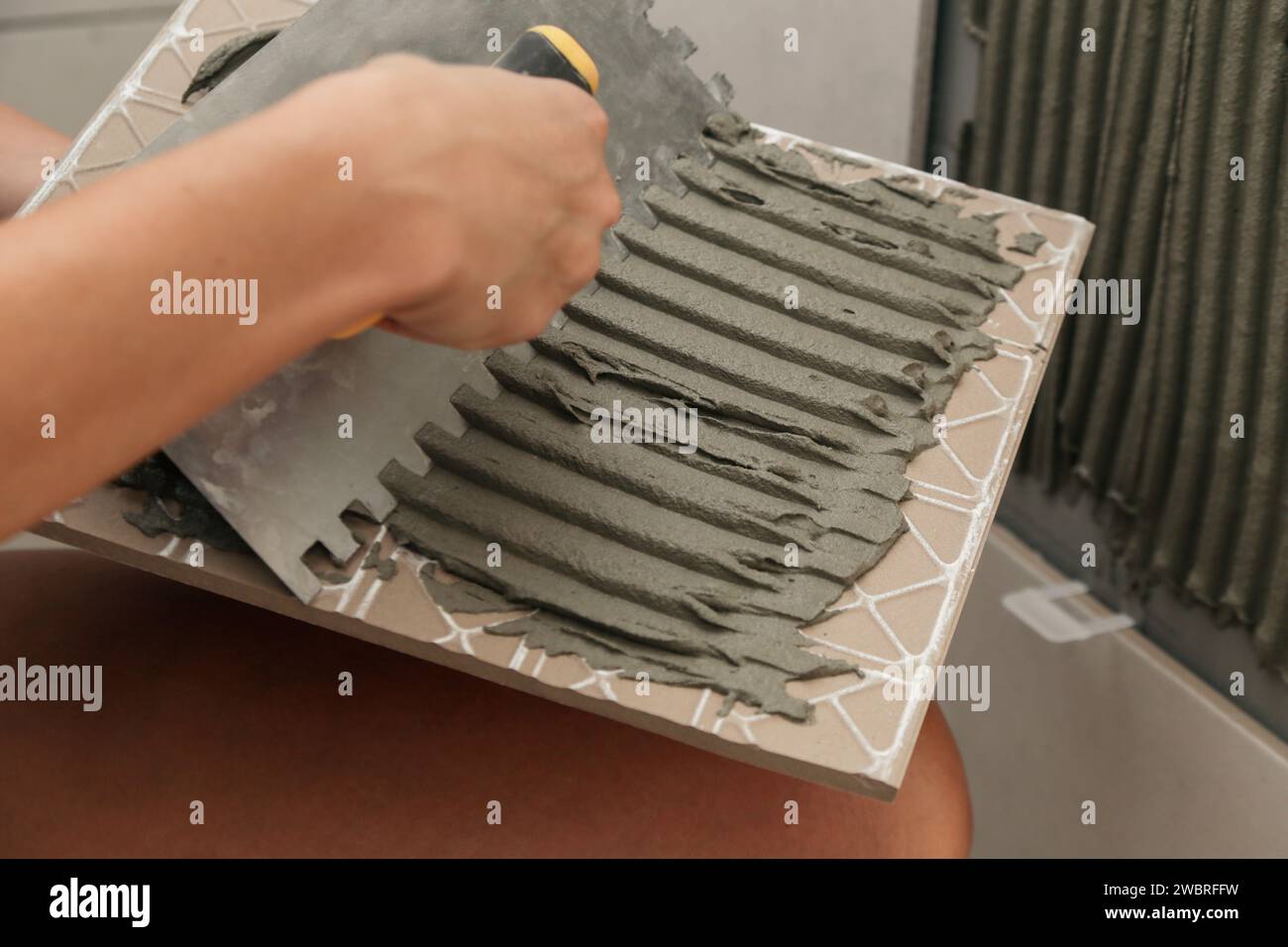 Woman tiling bathroom walls, applying adhesive on a tile and placing ...